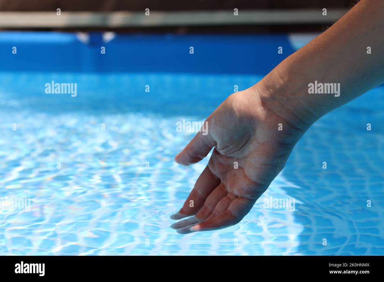 The fingers of right-hand touching the water of a pool under the ...