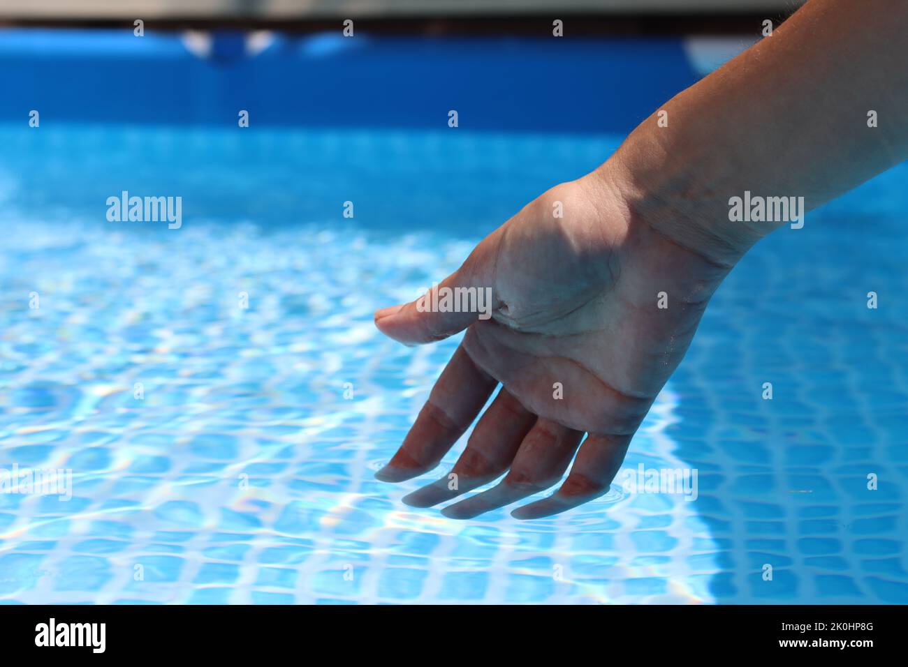 The fingers of right-hand touching the water of a pool under the ...