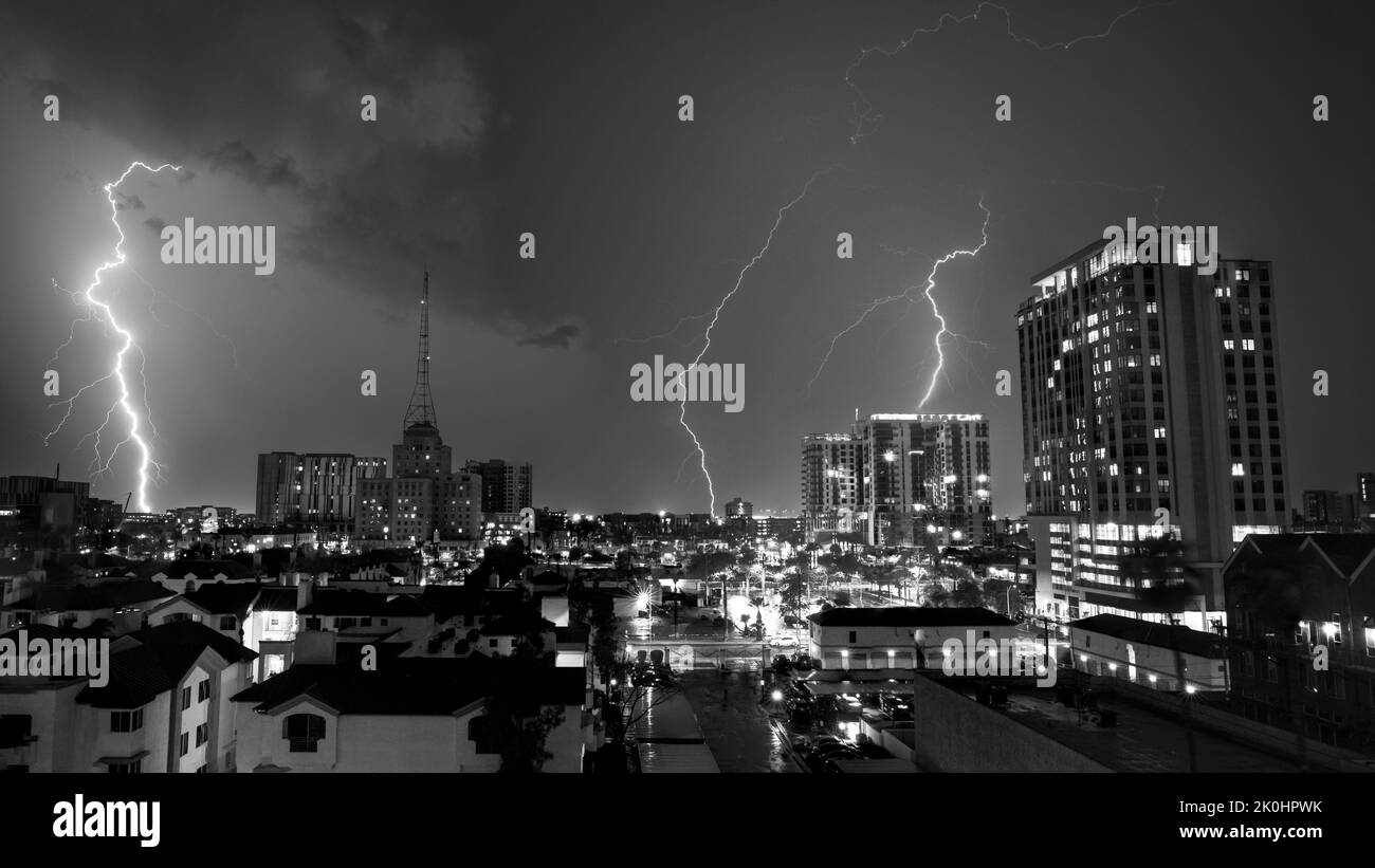 A grayscale of striking lightning at night in an illuminated city of ...