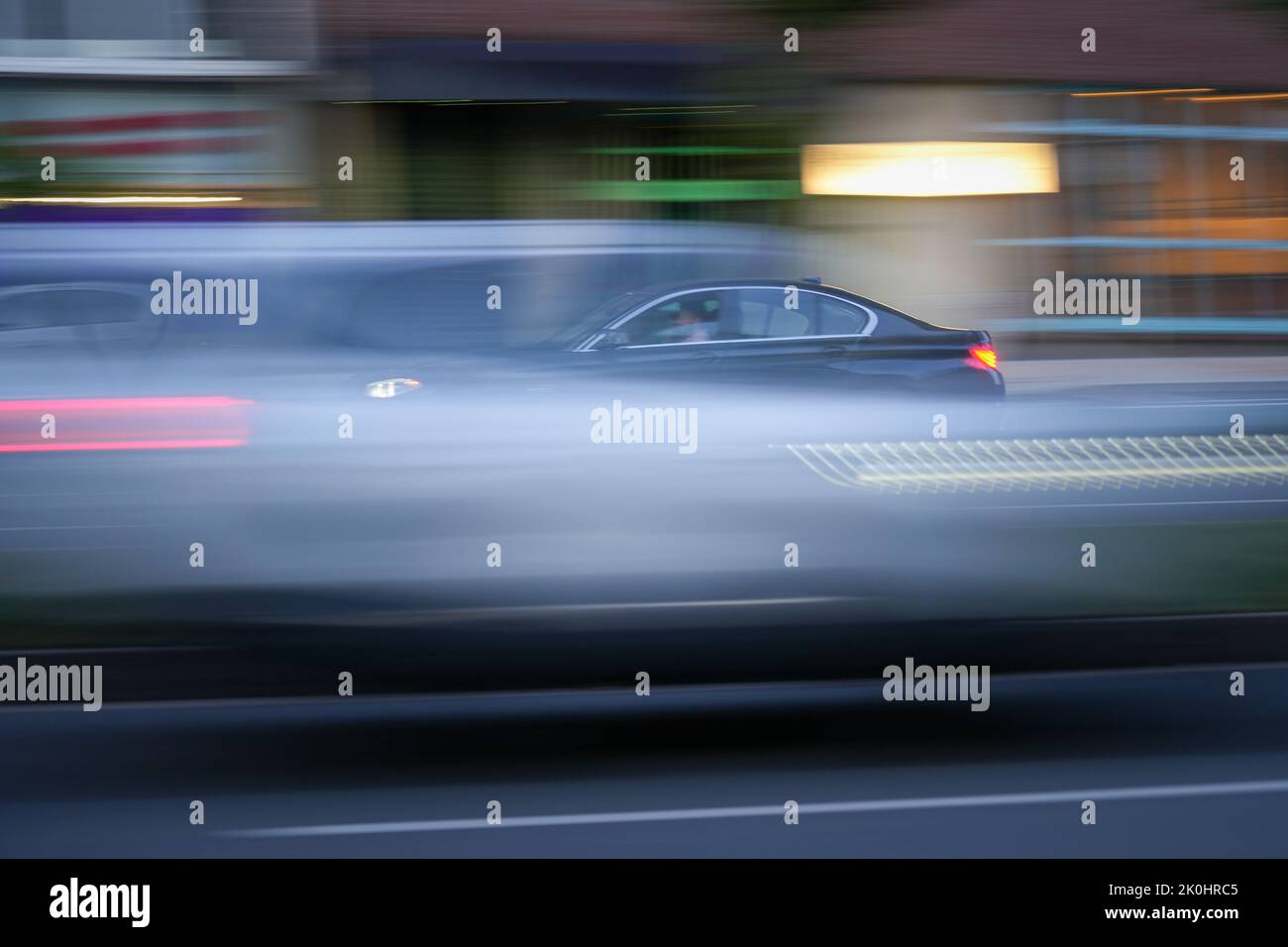 A black car driving fast on a road, with lights of the long exposure ...