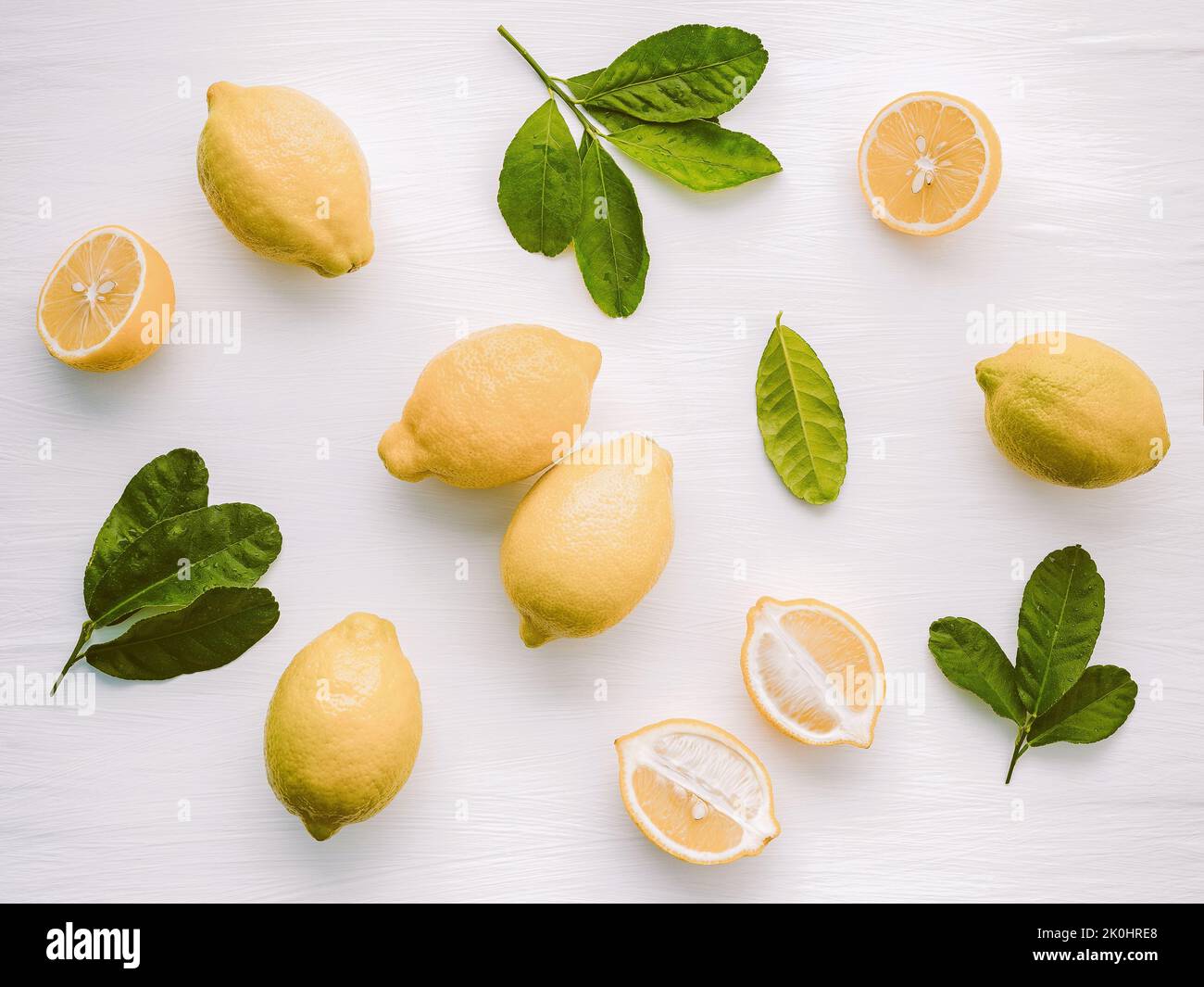 A top view of fresh juice lemons and green leaves on a white surface ...