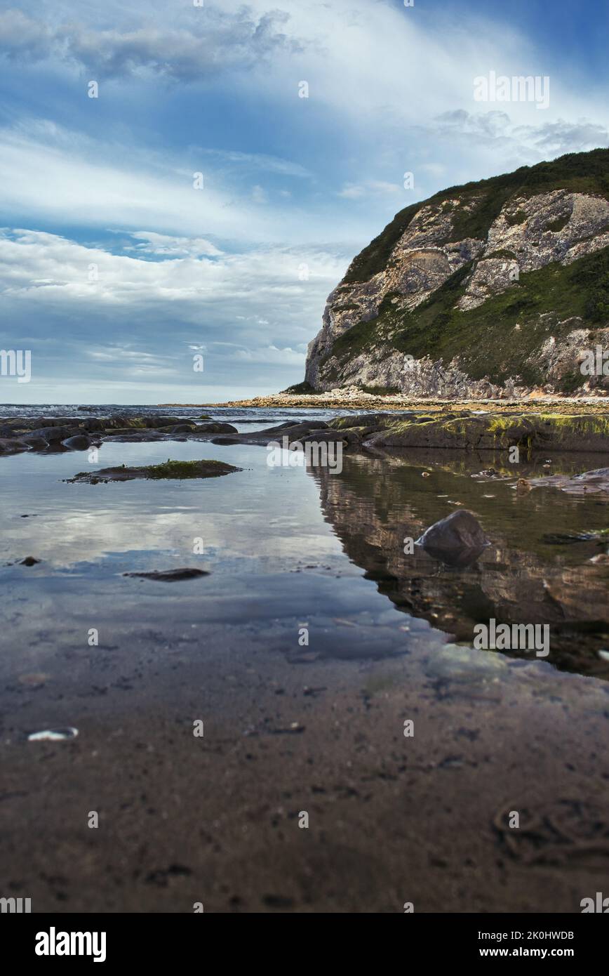 A vertical view of the cliff reflecting on the water under the cloudy ...