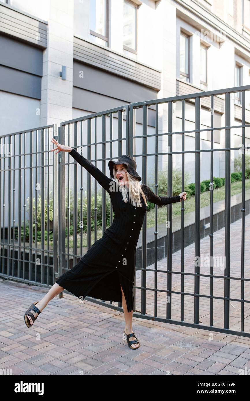 Posing blond woman covered in black clothes hanging on a rail fence in ...