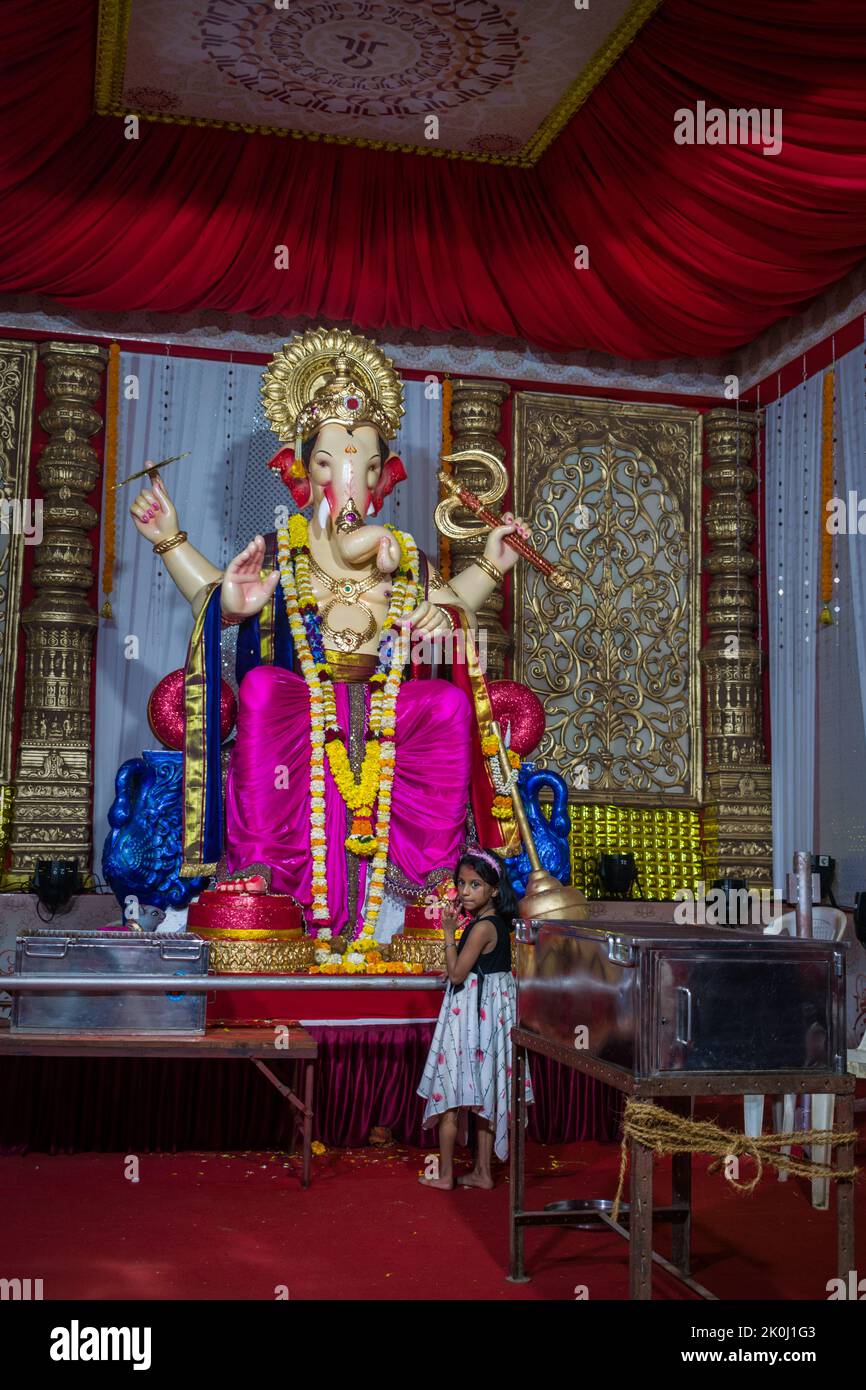 A girl praying before a beautiful idol of Lord Ganesha at a mandal in ...