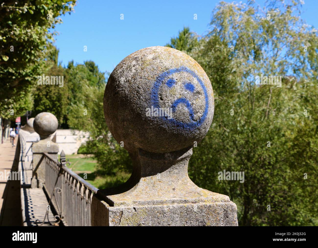 Sprayed blue paint sad face graffiti on stone ball fence cap next to ...