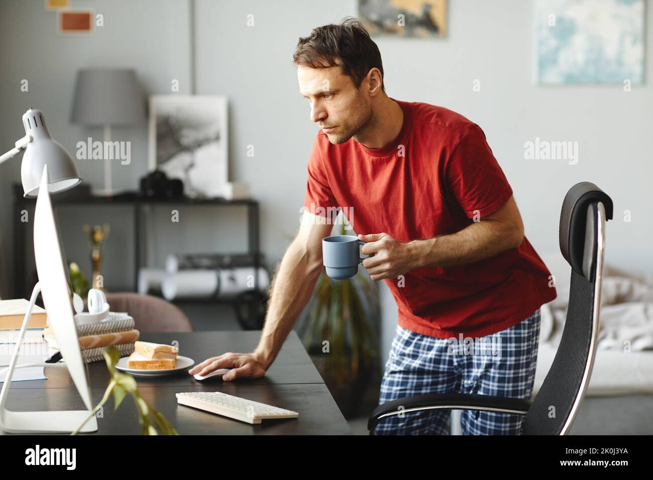 Young man drinking coffee and checking email on his computer at table ...