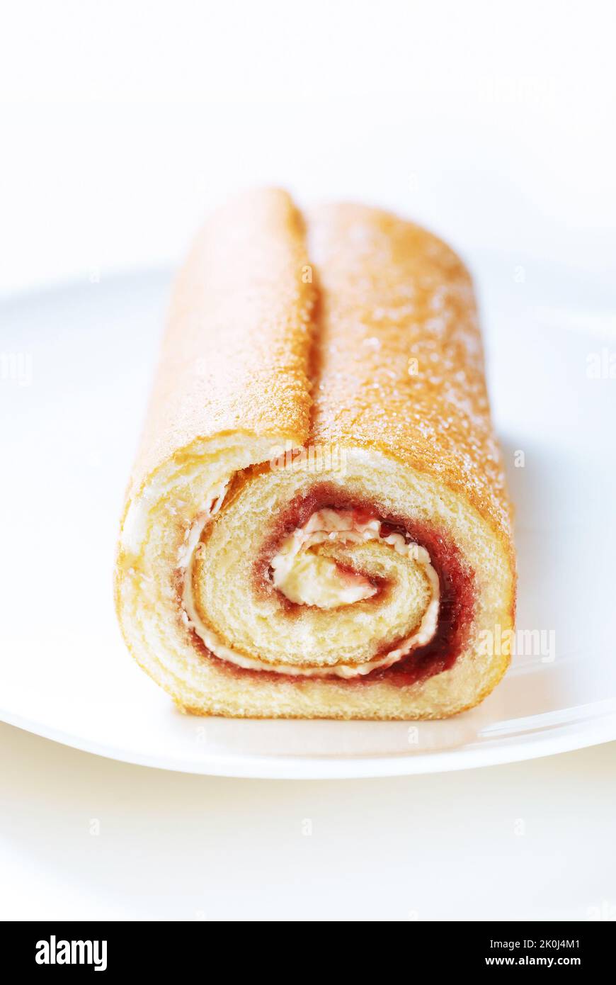 A swiss roll with strawberry jam and cream filling on a white plate ...