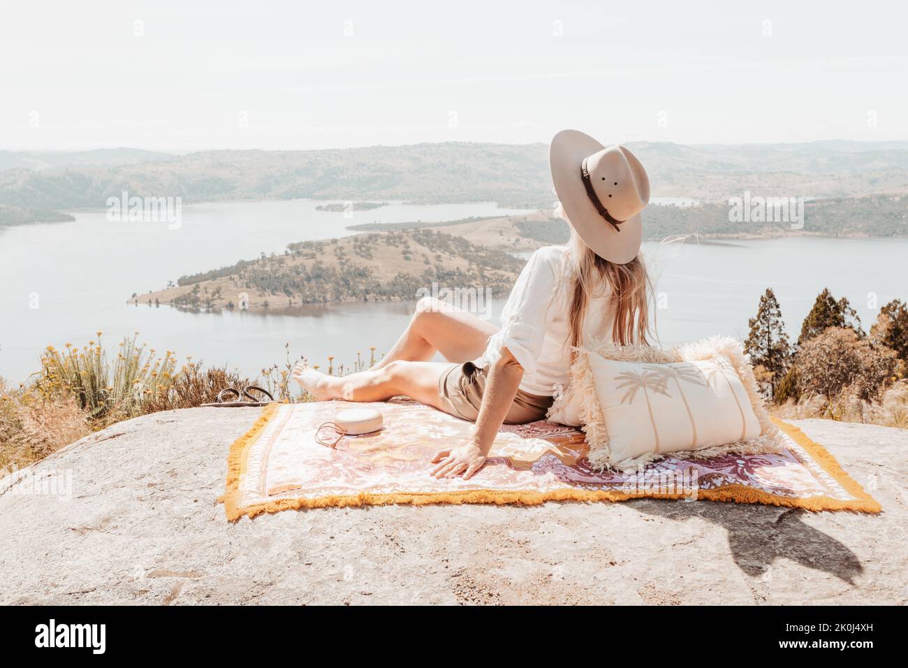 Woman siting relaxing on woven fringed picnic rug high above with ...