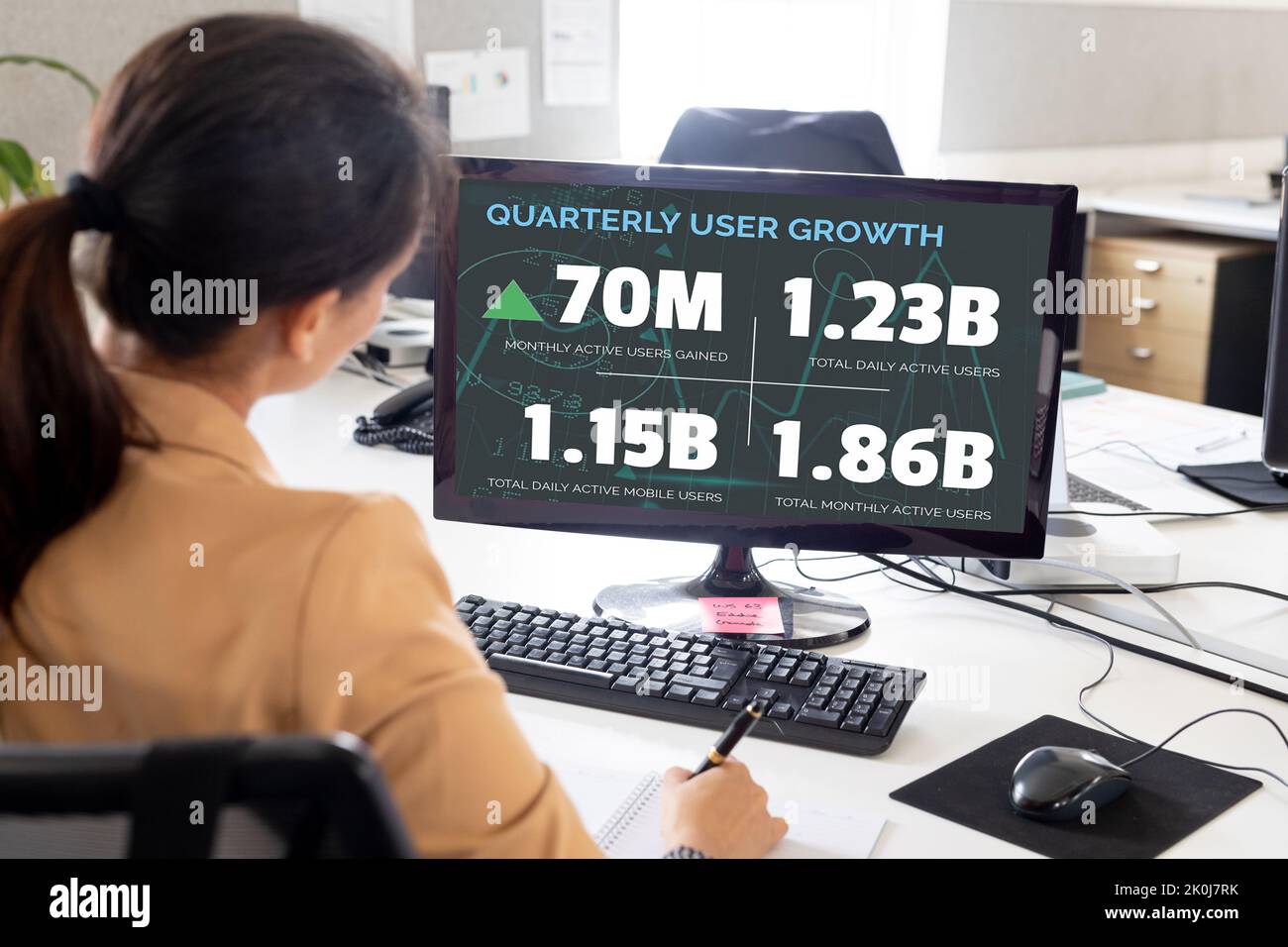 Over shoulder view of asian businesswoman using computer with user growth figures on screen ...