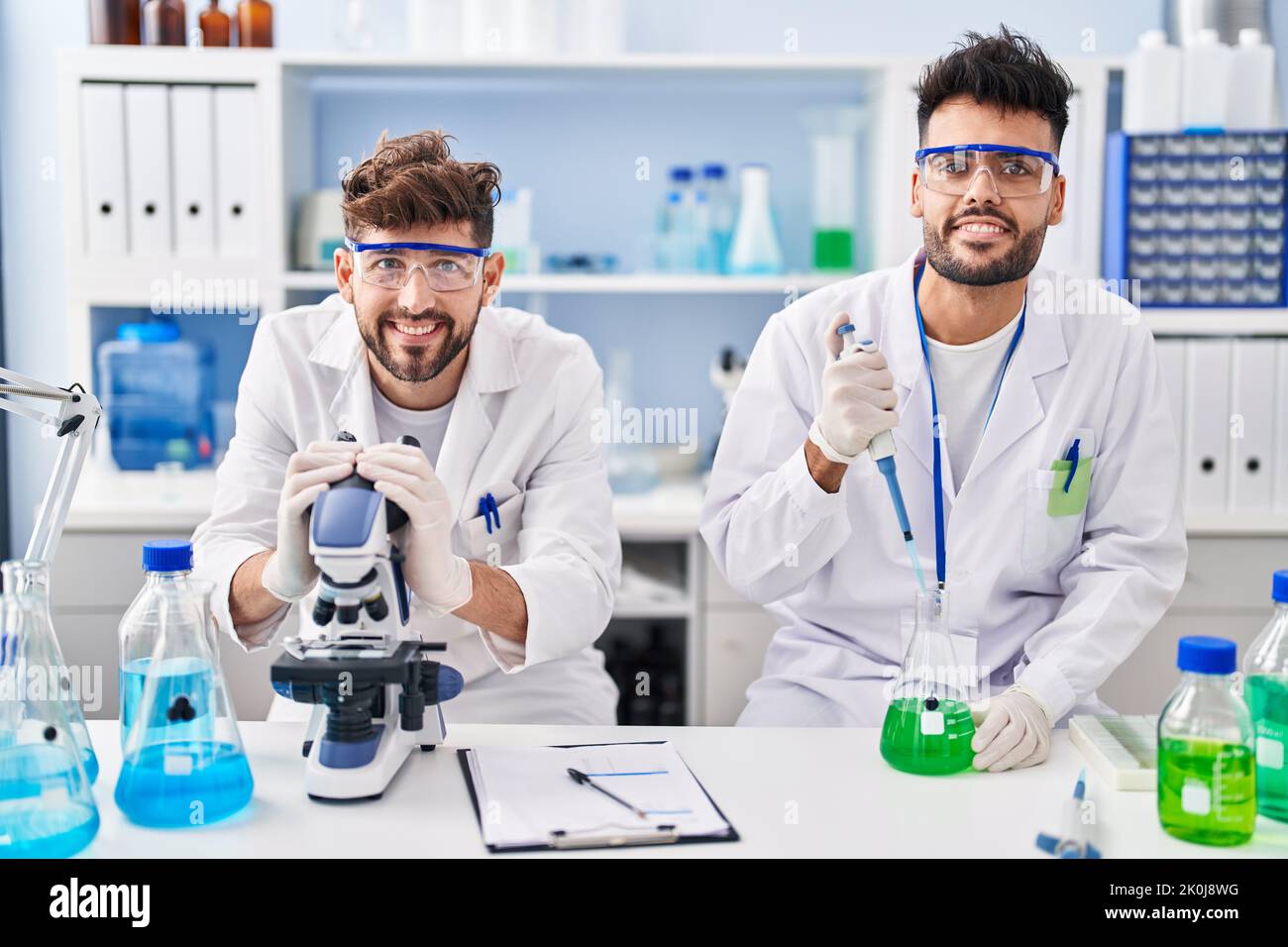 Young couple wearing scientist uniform using microscope and pipette at ...