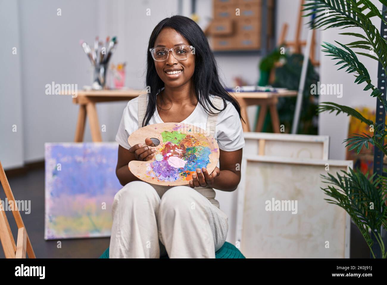 African young woman holding painter palette looking positive and happy ...