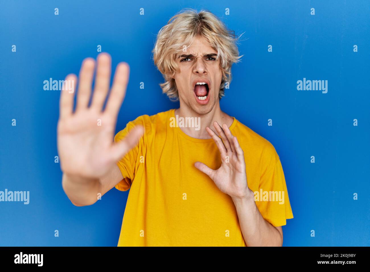 Young modern man standing over blue background afraid and terrified ...