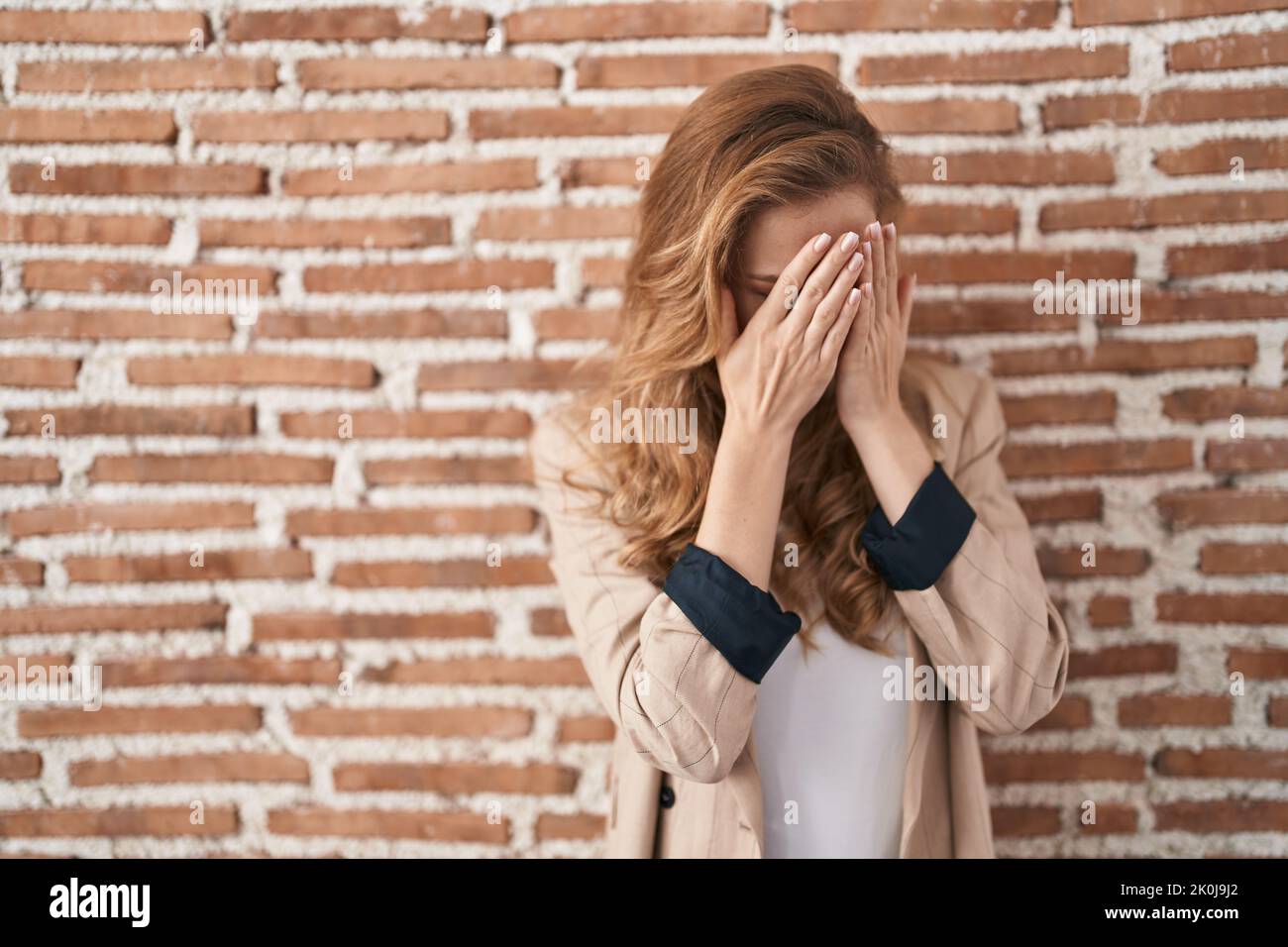 Beautiful blonde woman standing over bricks wall with sad expression ...