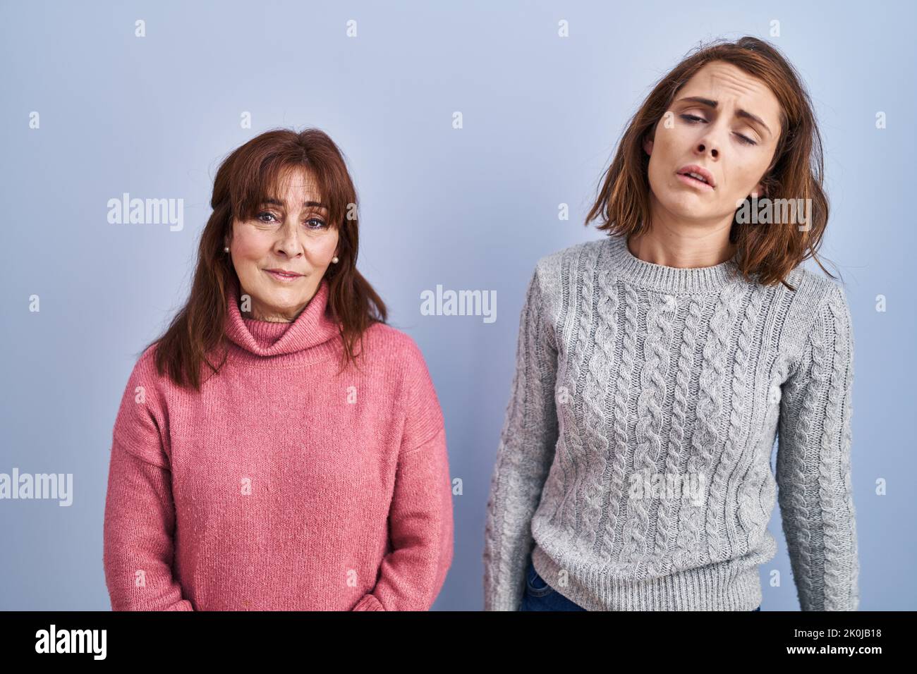 Mother and daughter standing over blue background looking sleepy and ...