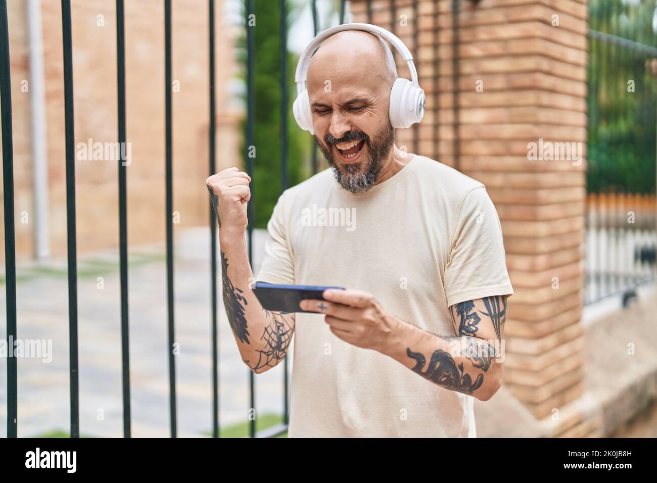 Young bald man smiling confident playing video game at street Stock ...