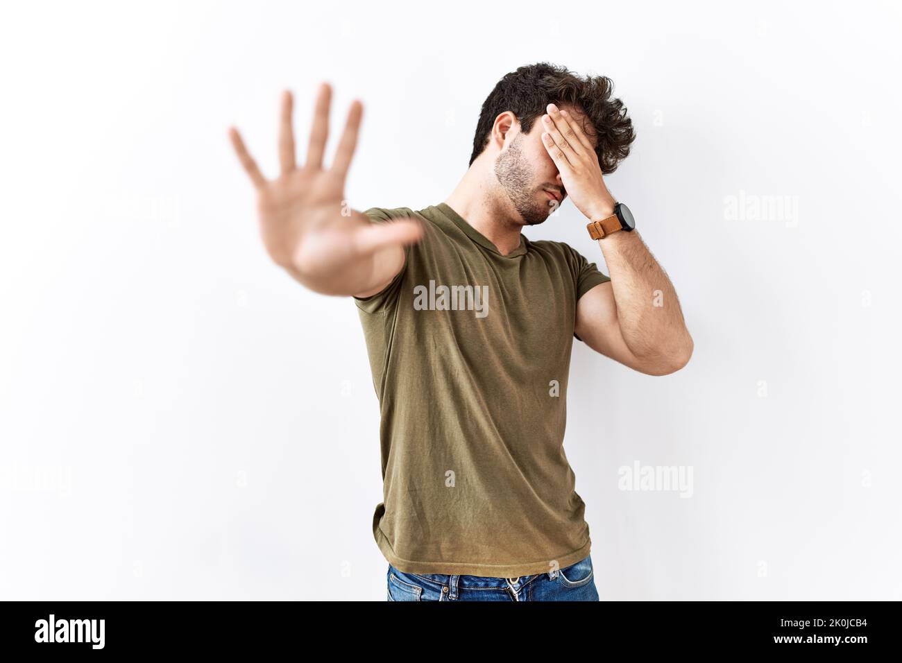 Hispanic man standing over isolated white background covering eyes with ...