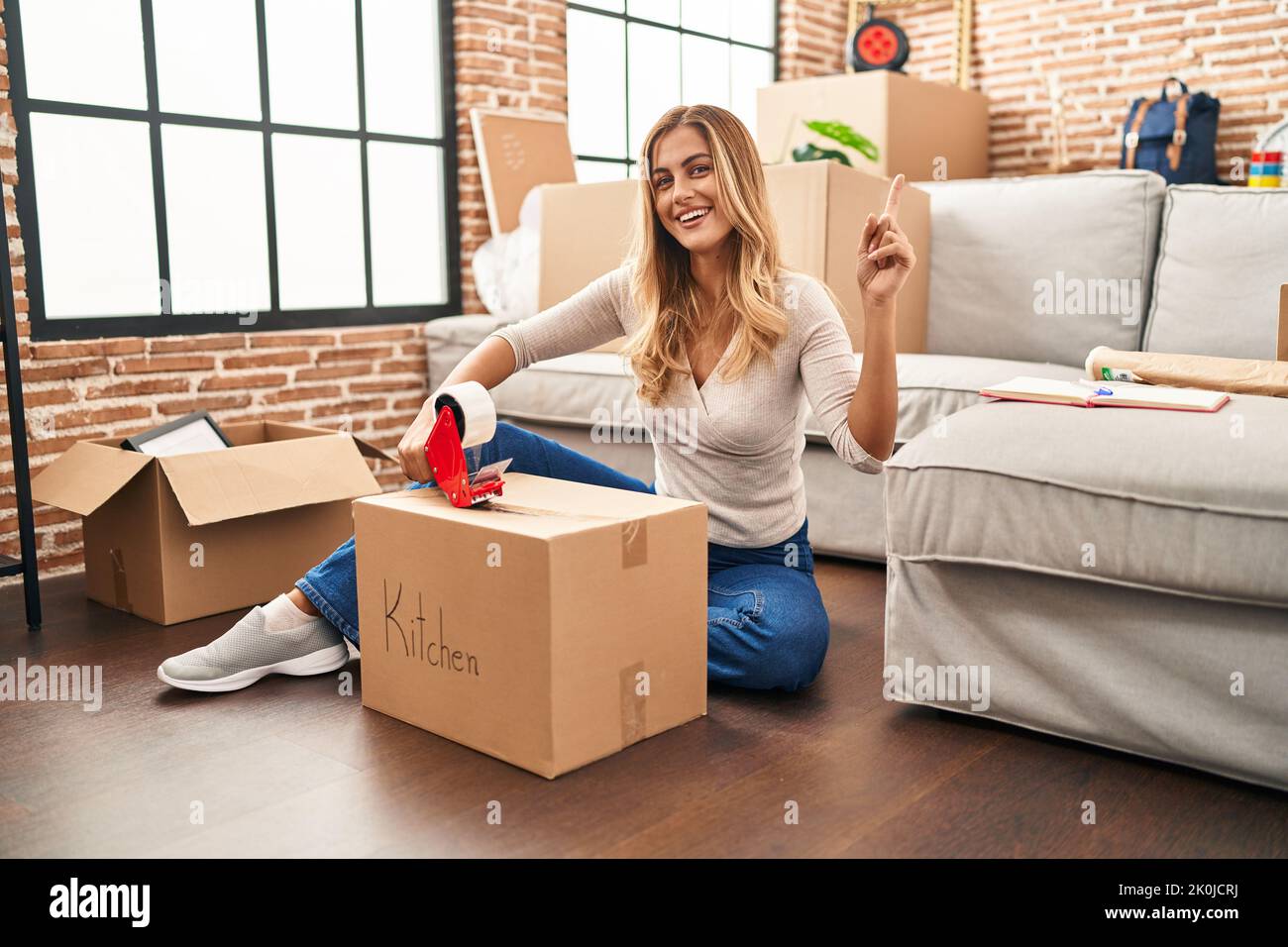 Young blonde woman sitting on the floor closing boxes home smiling ...