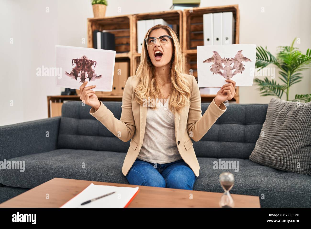 Young blonde therapist woman holding rorschach test angry and mad ...