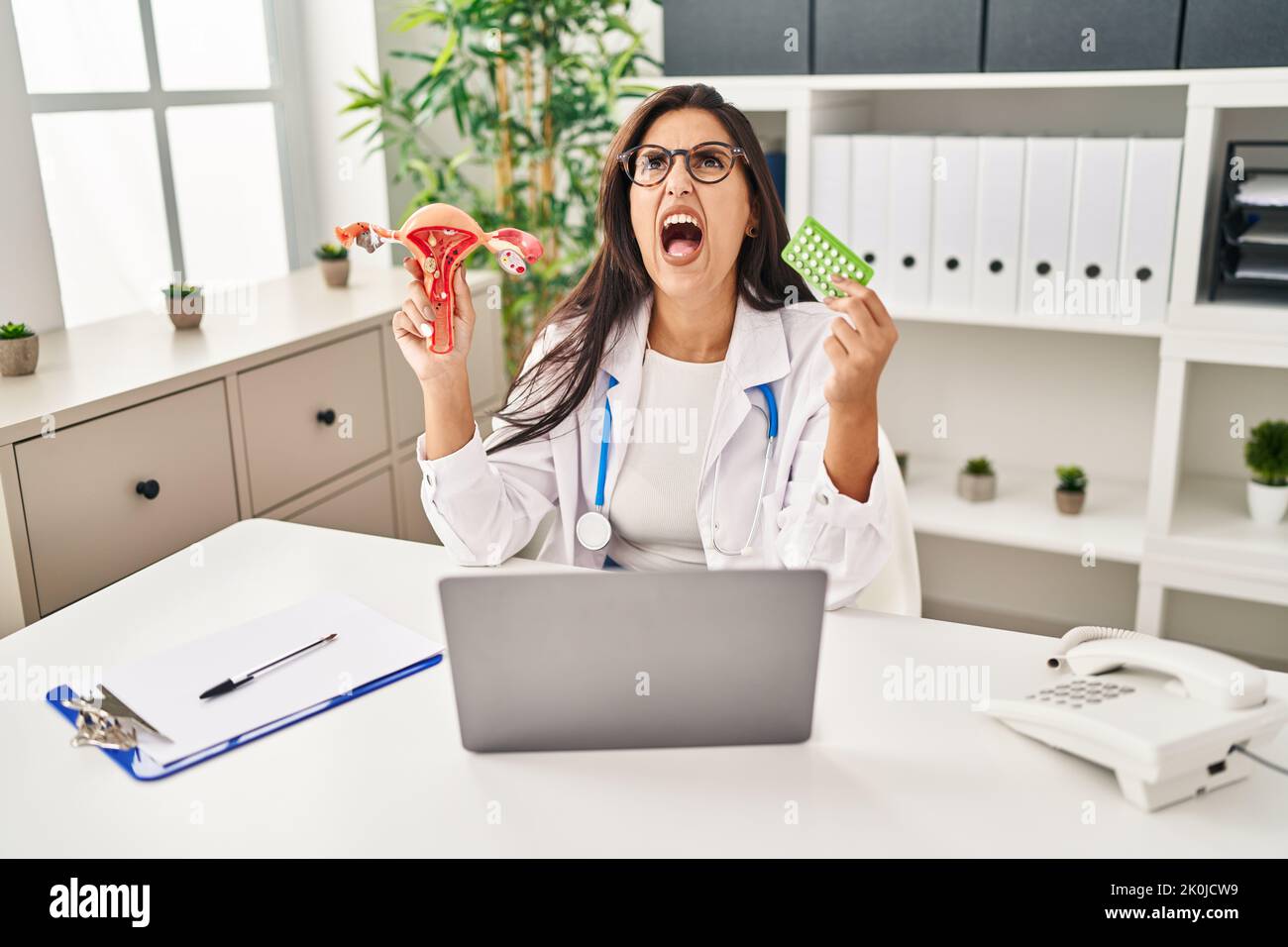 Young hispanic doctor woman holding anatomical female genital organ and ...
