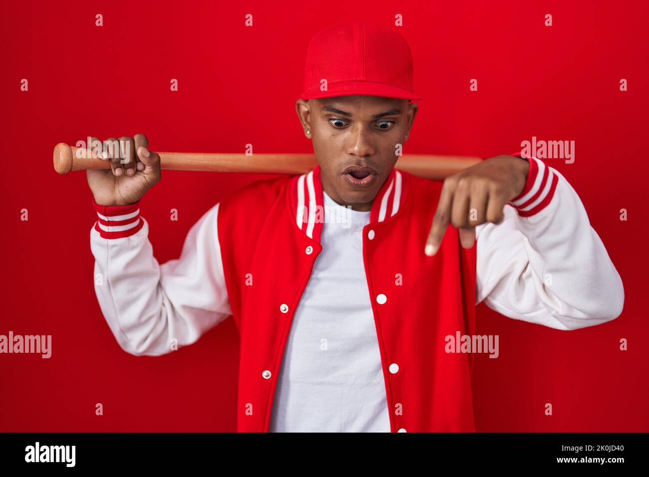 Young hispanic man playing baseball holding bat pointing down with ...
