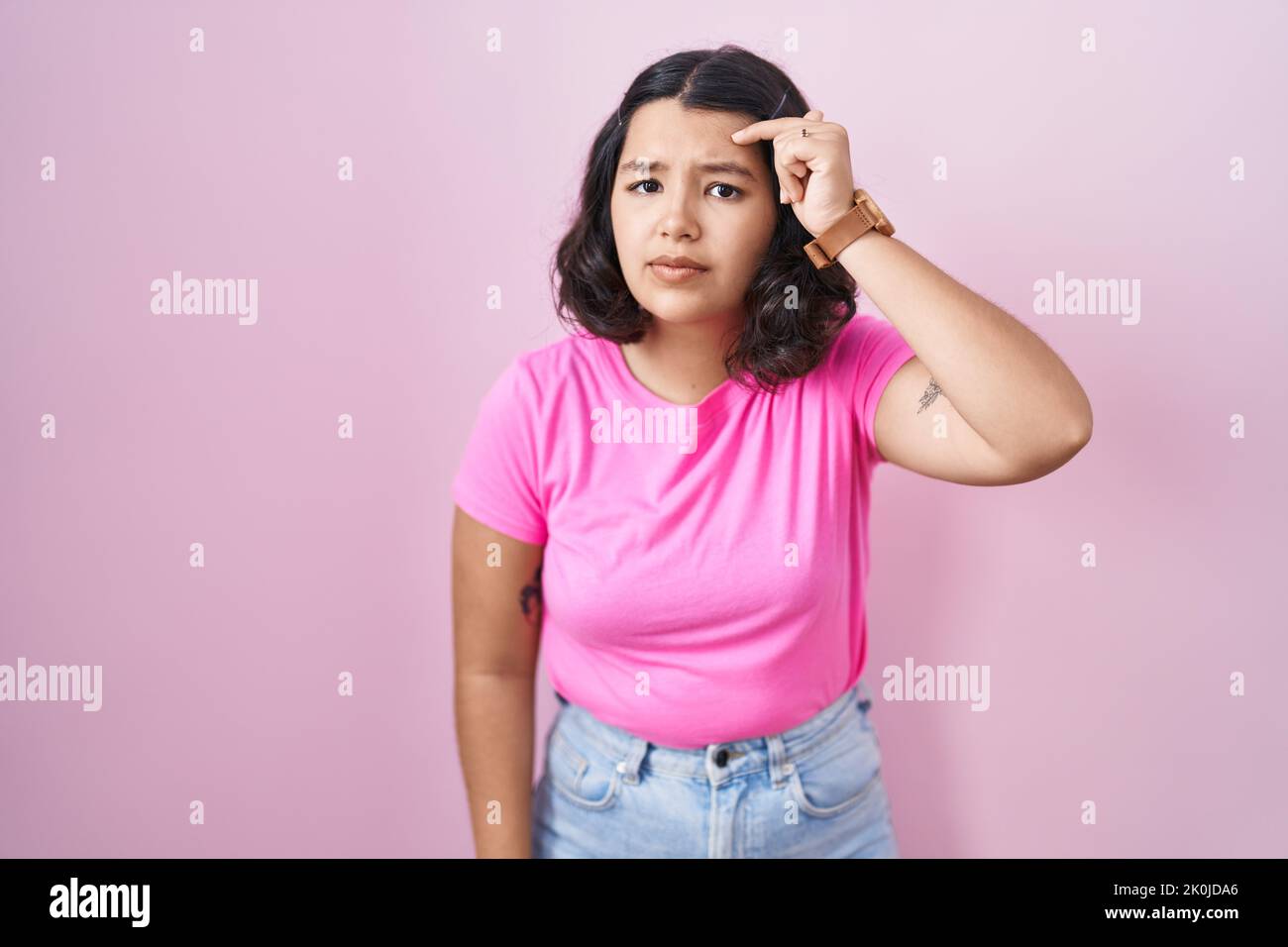 Young hispanic woman standing over pink background pointing unhappy to ...