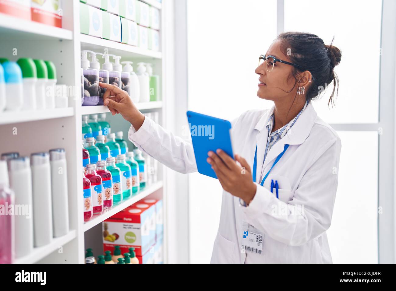 Young beautiful hispanic woman pharmacist using touchpad working at ...
