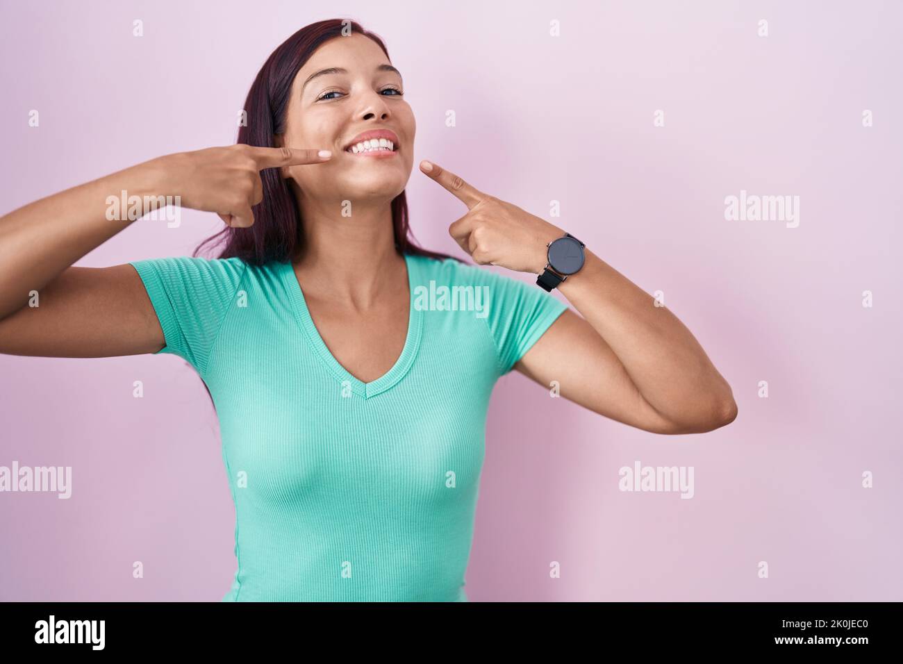 Young hispanic woman standing over pink background smiling cheerful ...