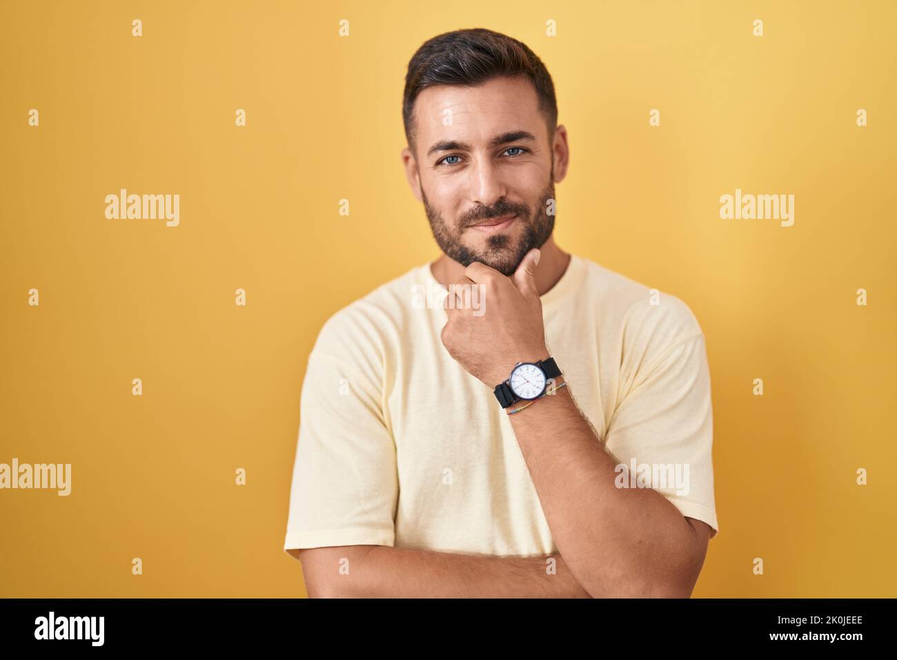Handsome hispanic man standing over yellow background looking confident ...