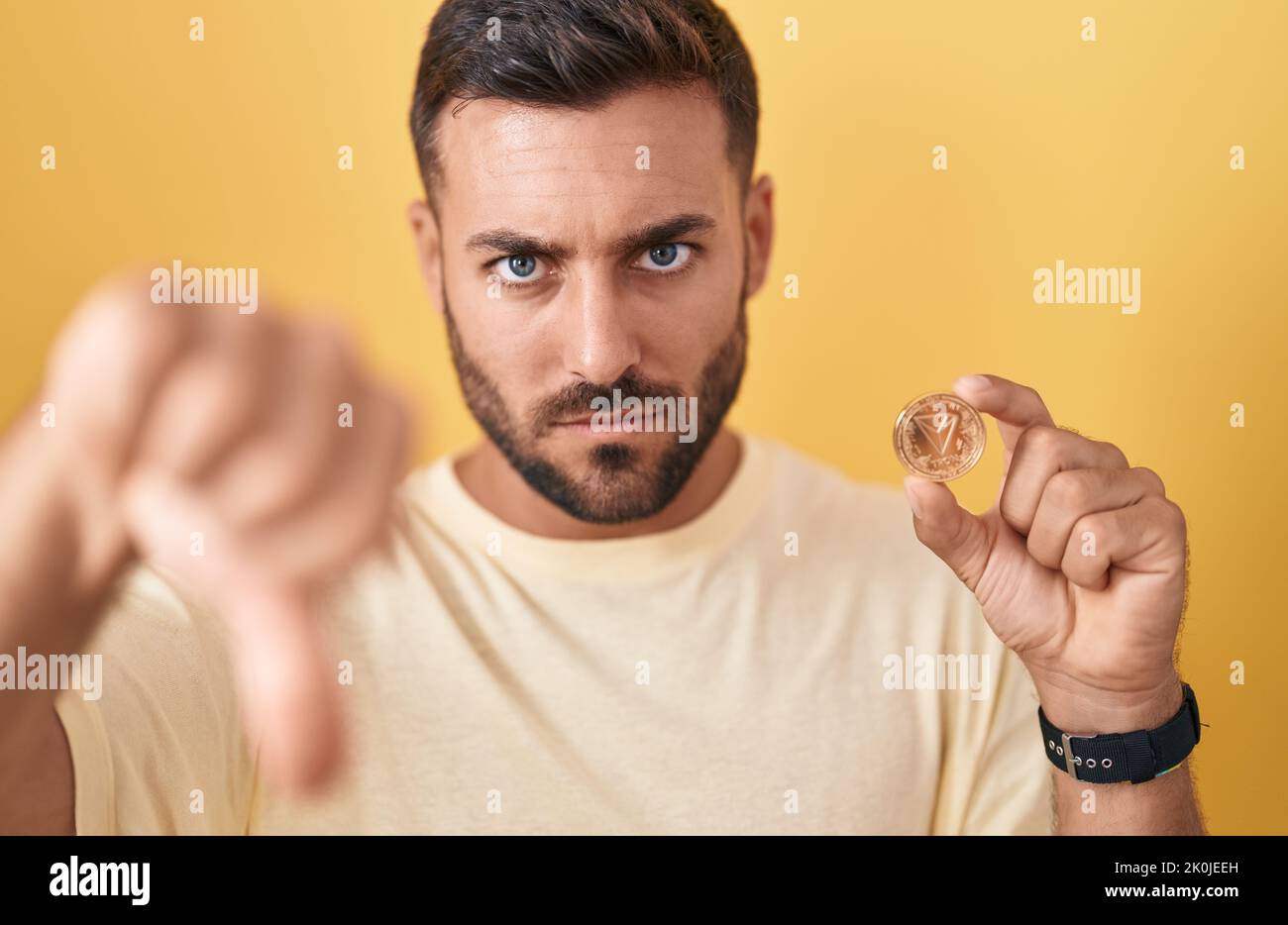 Handsome hispanic man holding tron cryptocurrency coin with angry face ...