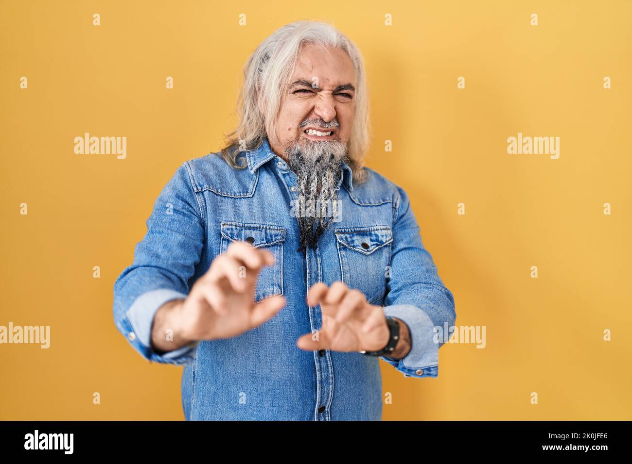 Middle age man with grey hair standing over yellow background disgusted ...