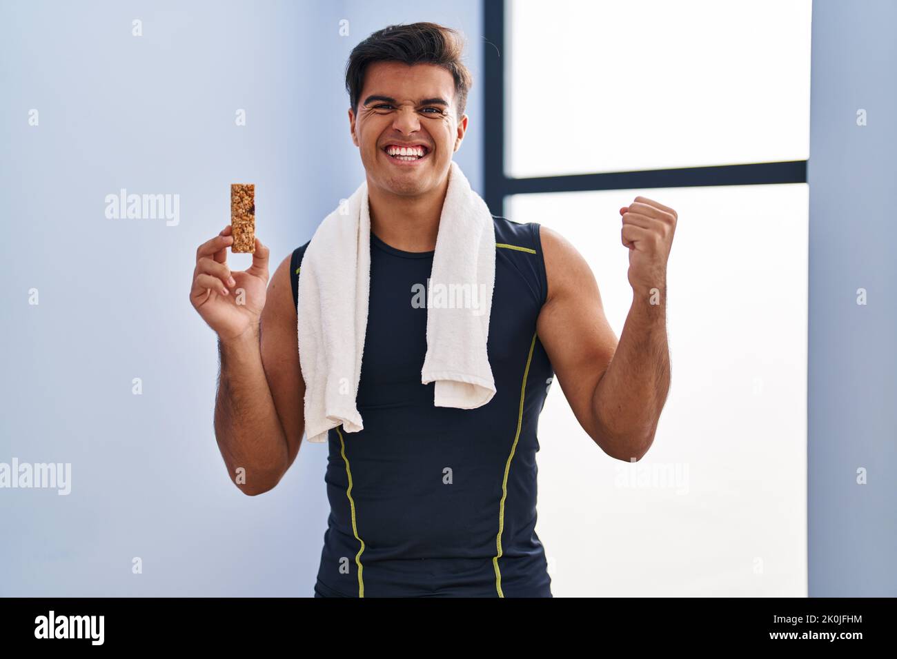 Hispanic man eating protein bar as healthy energy snack screaming proud ...