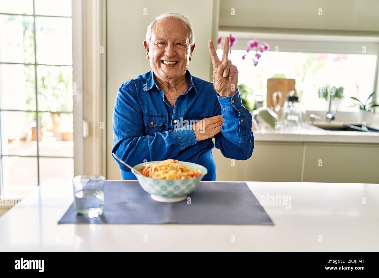 Senior man with grey hair eating pasta spaghetti at home smiling with ...