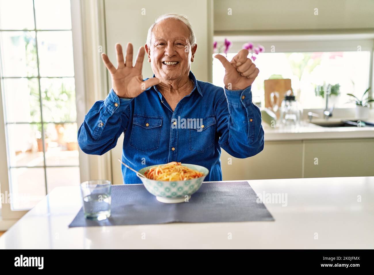 Senior man with grey hair eating pasta spaghetti at home showing and ...