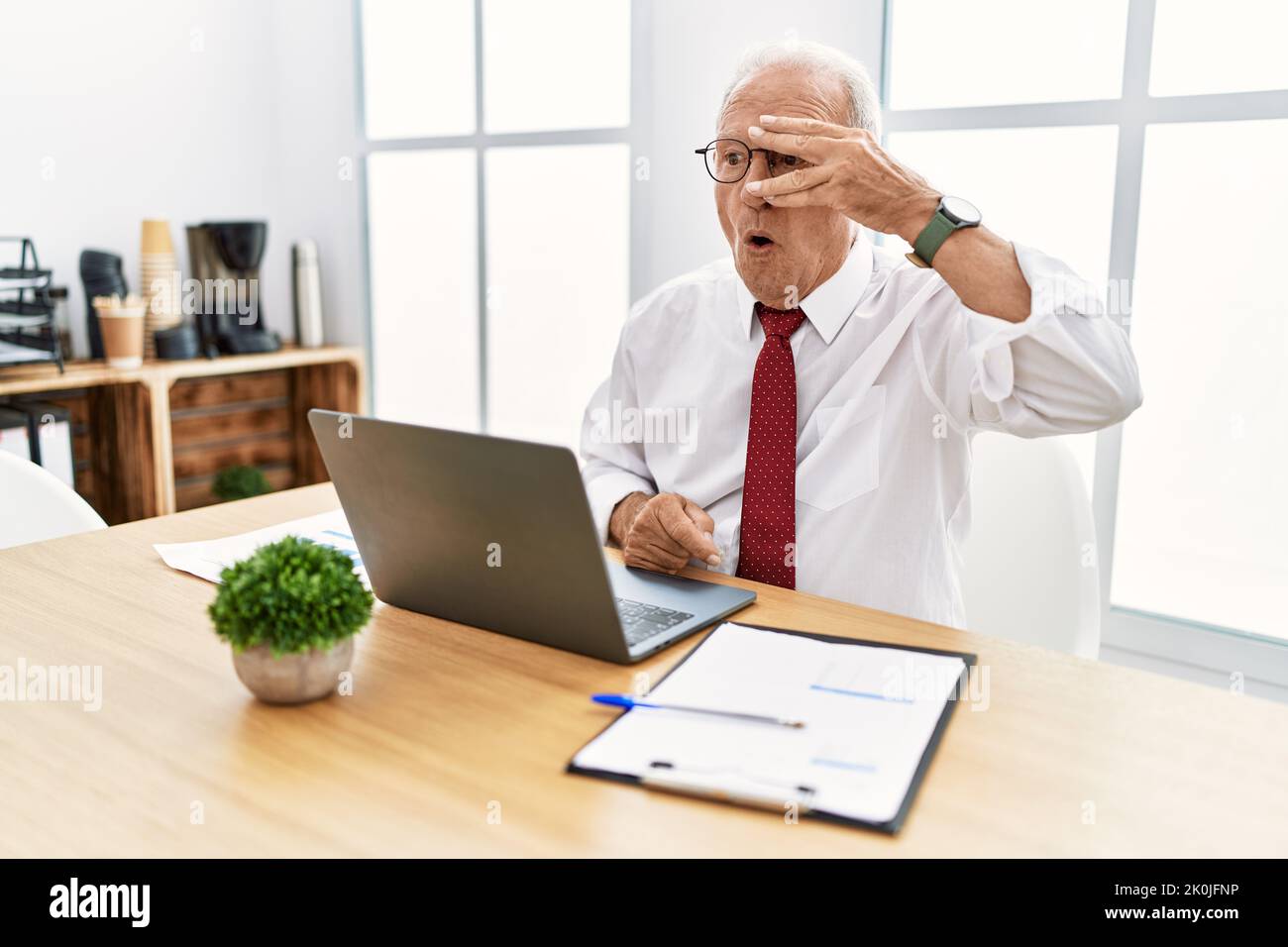 Senior man working at the office using computer laptop peeking in shock ...