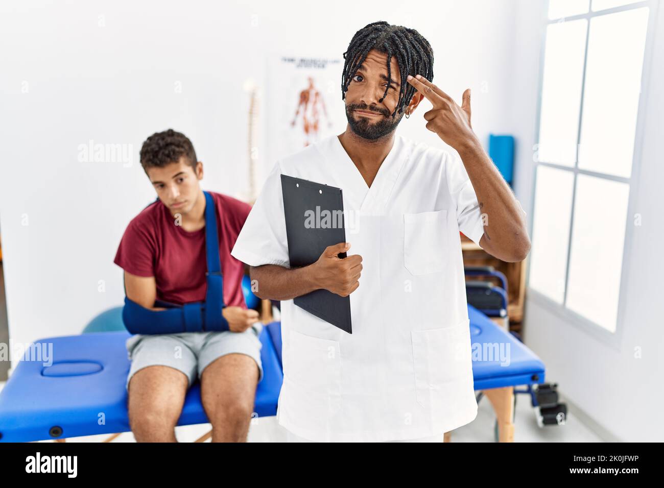 Young hispanic man working at pain recovery clinic with a man with ...