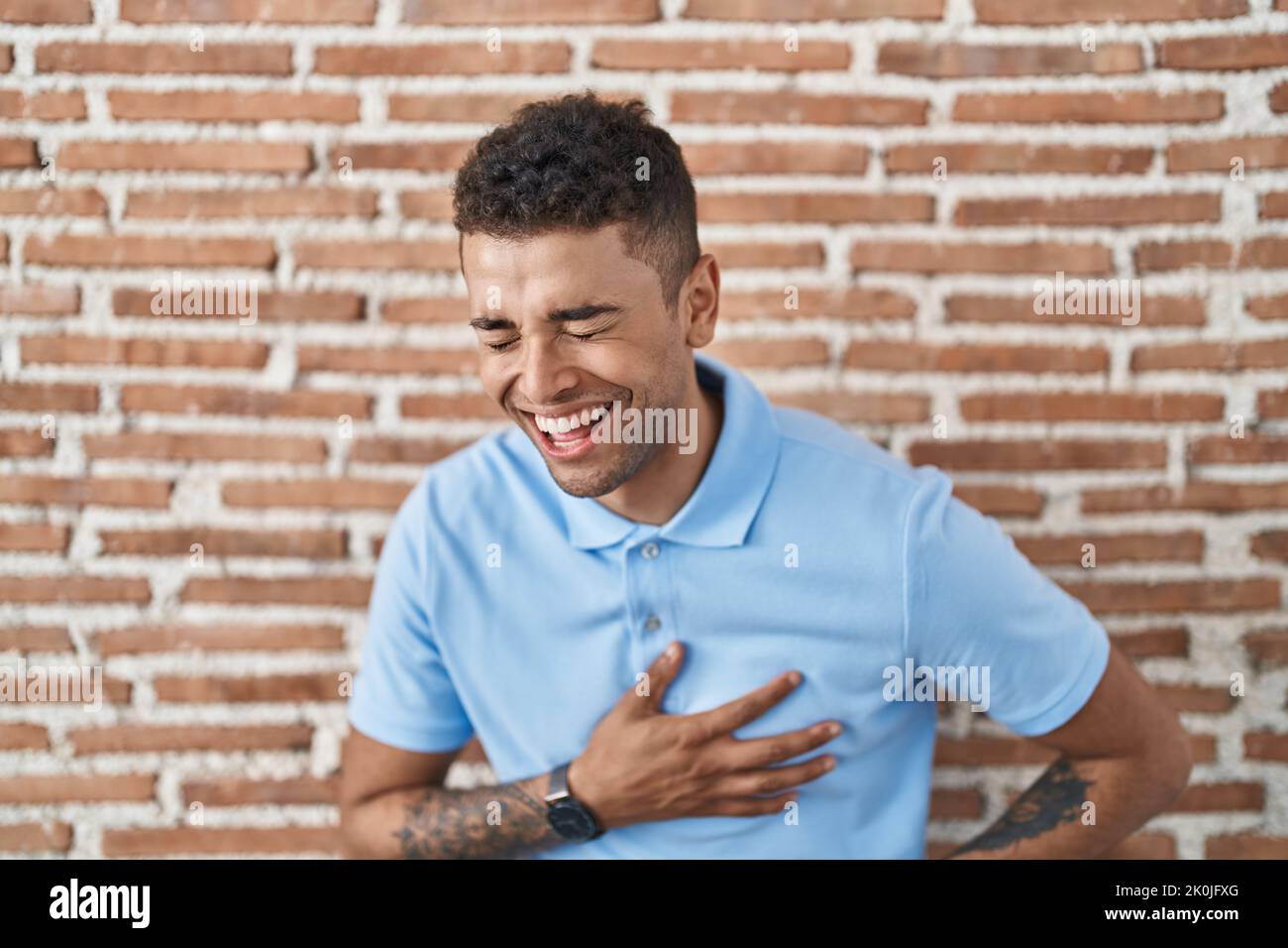 Brazilian young man standing over brick wall smiling and laughing hard ...