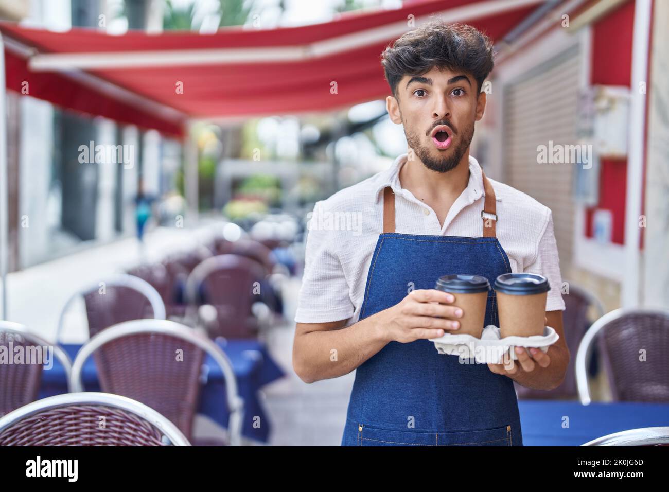 Arab man with beard wearing waiter apron at restaurant terrace scared ...
