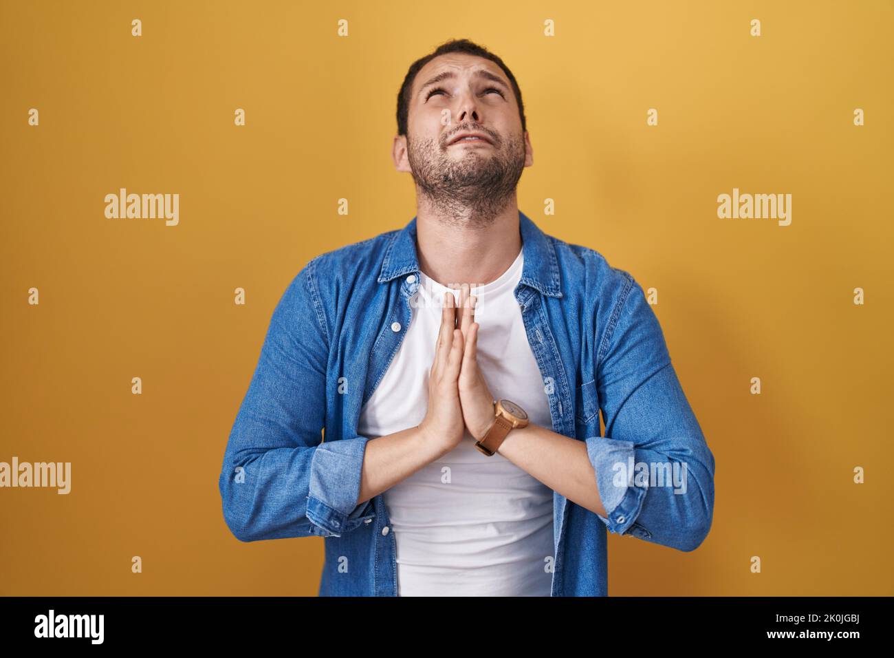 Hispanic man standing over yellow background begging and praying with ...