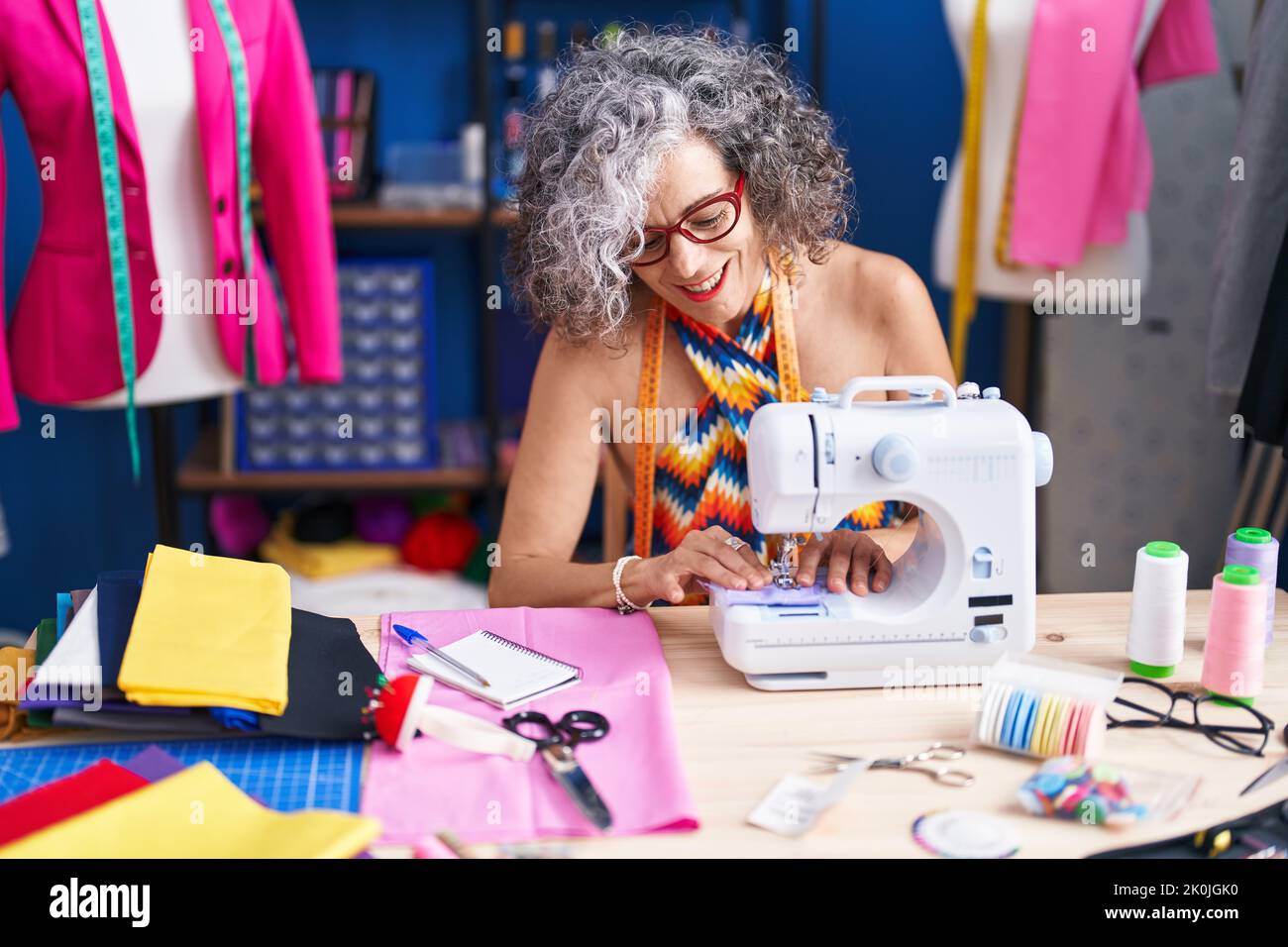 Middle age grey-haired woman tailor smiling confident using sewing ...