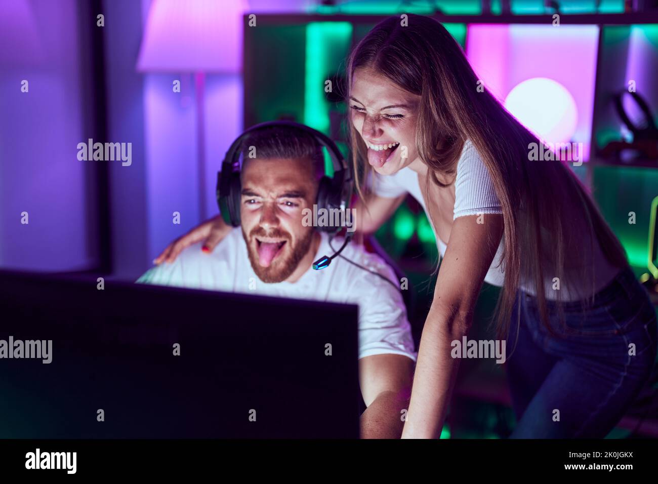 Young couple playing video games sticking tongue out happy with funny ...