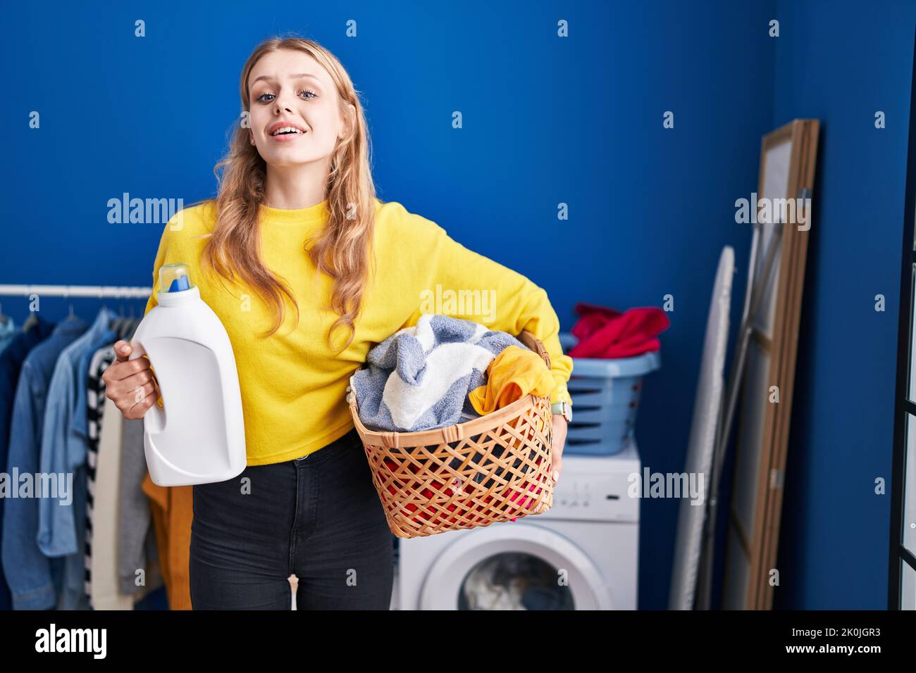 Young caucasian woman holding laundry basket and detergent bottle celebrating crazy and amazed ...