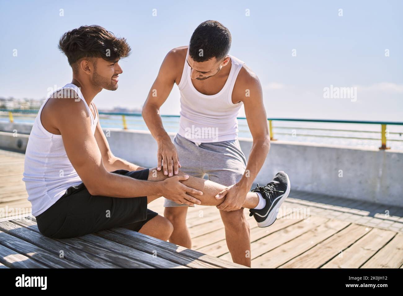 Two hispanic men sporty couple sitting on bench for leg injury at ...