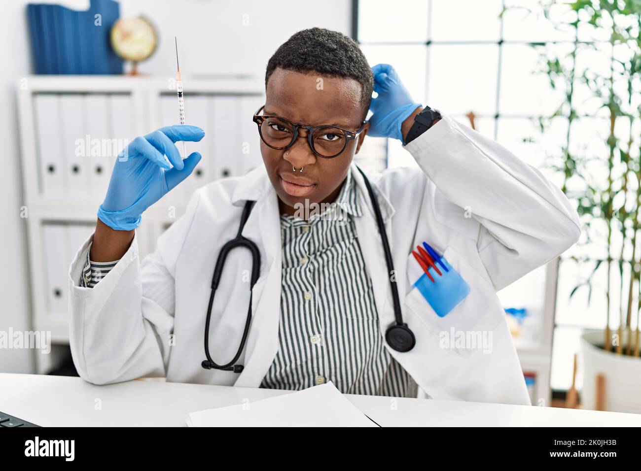 Young african doctor man holding syringe at the hospital confuse and ...