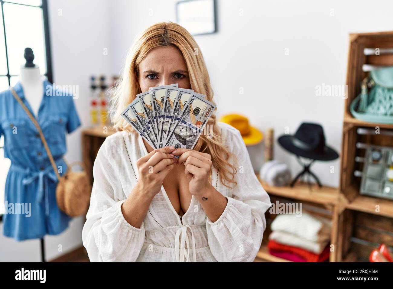 Beautiful blonde woman at retail boutique holding dollars banknotes ...