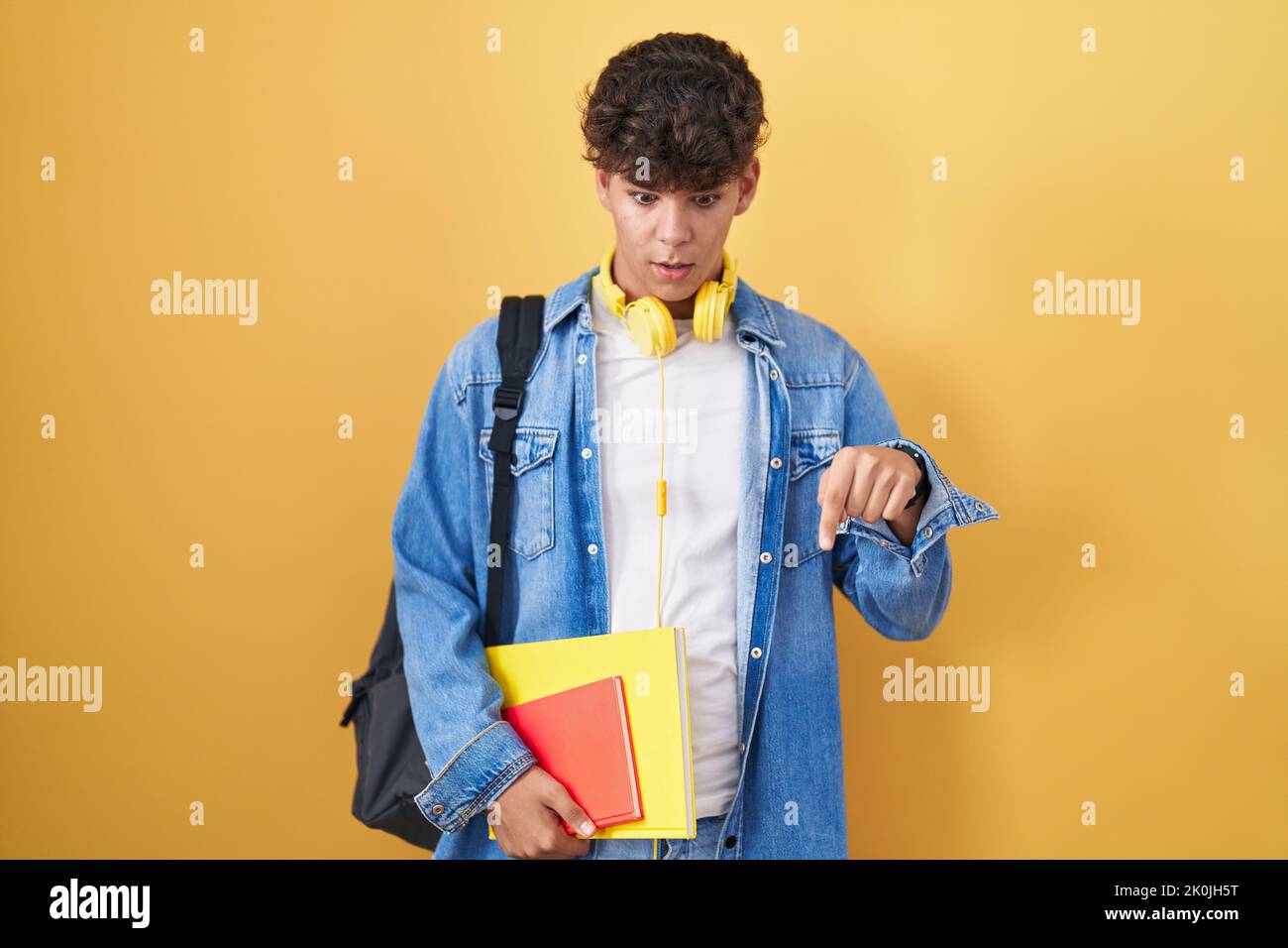 Hispanic teenager wearing student backpack and holding books pointing ...