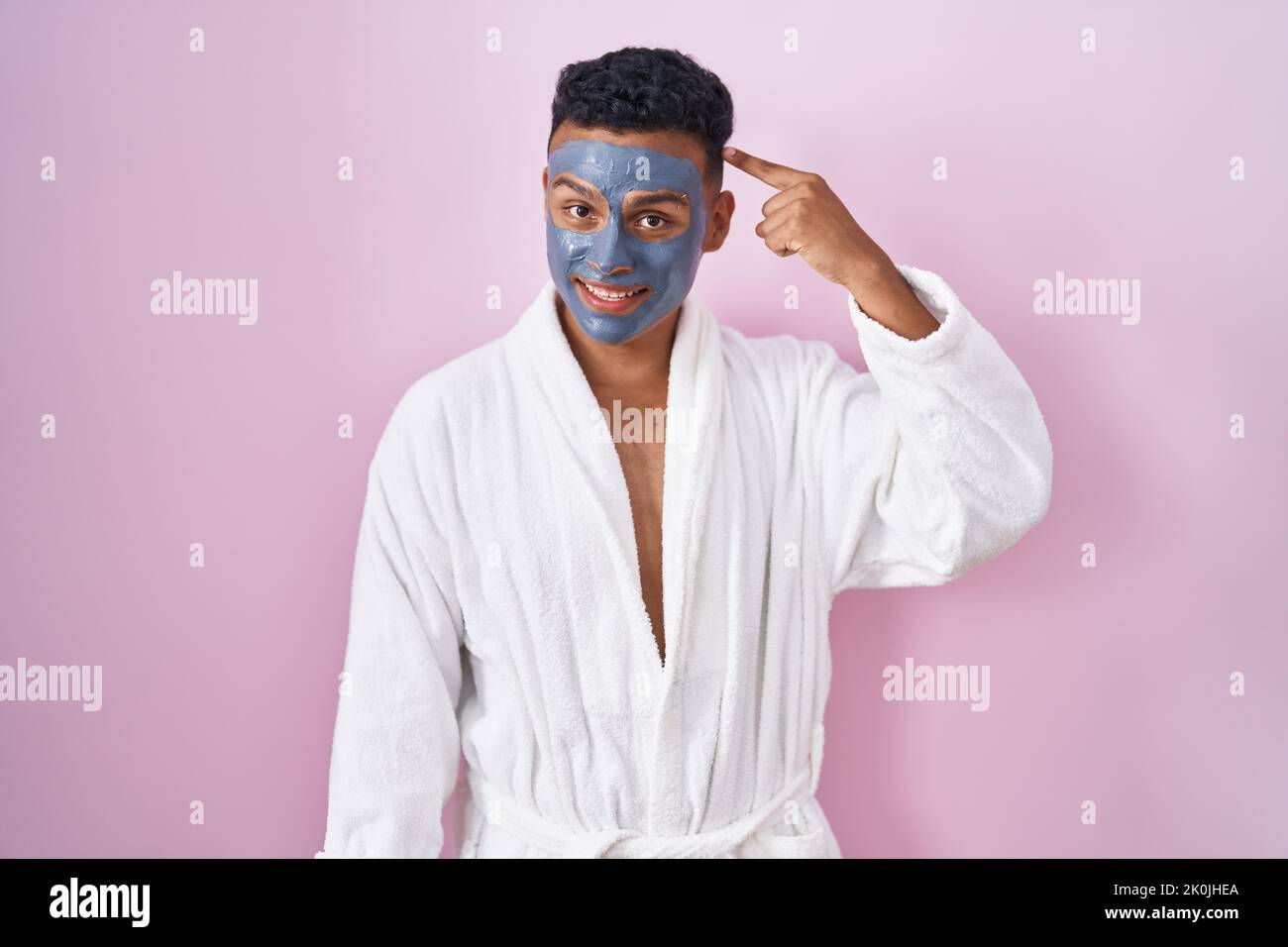 Young hispanic man wearing beauty face mask and bath robe smiling ...