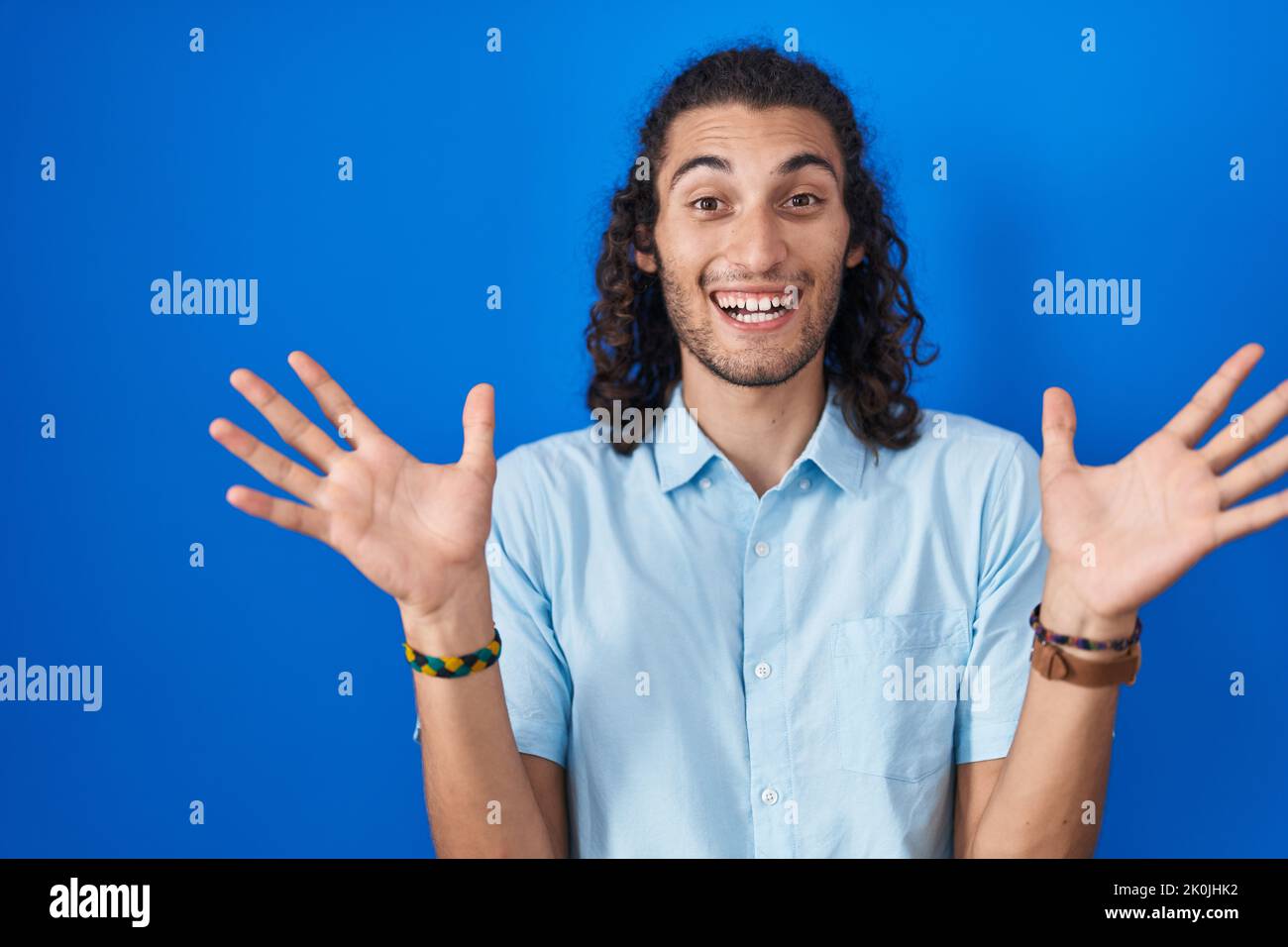 Young hispanic man standing over blue background celebrating crazy and ...