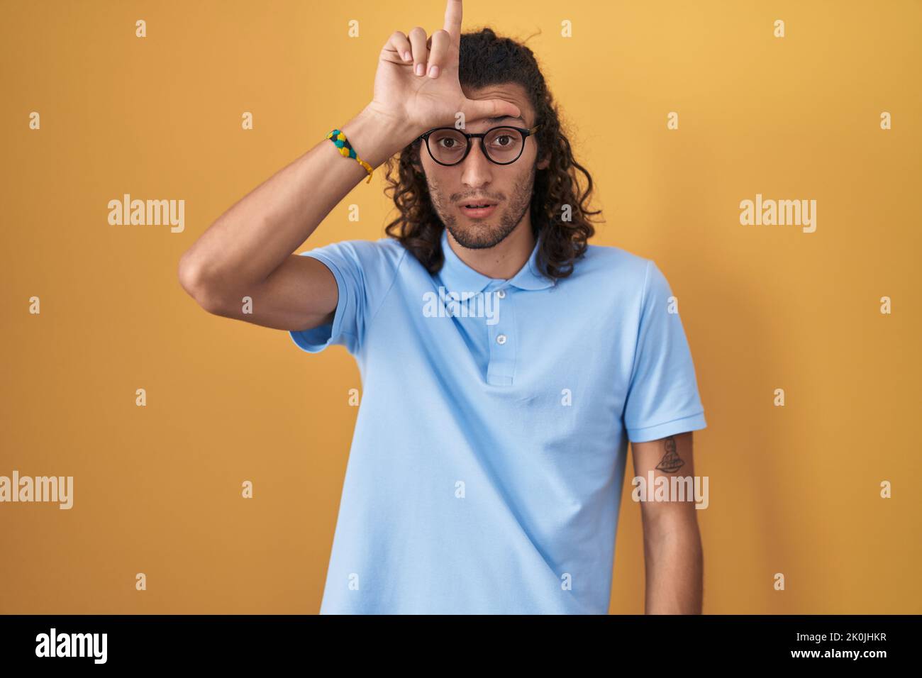 Young hispanic man standing over yellow background making fun of people ...