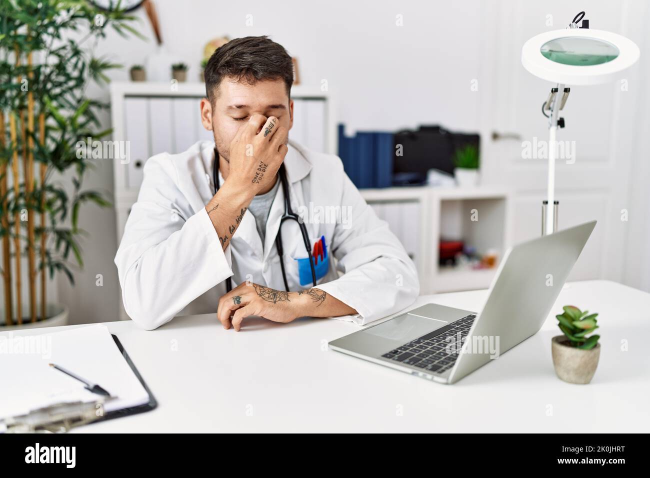 Young doctor working at the clinic using computer laptop tired rubbing ...