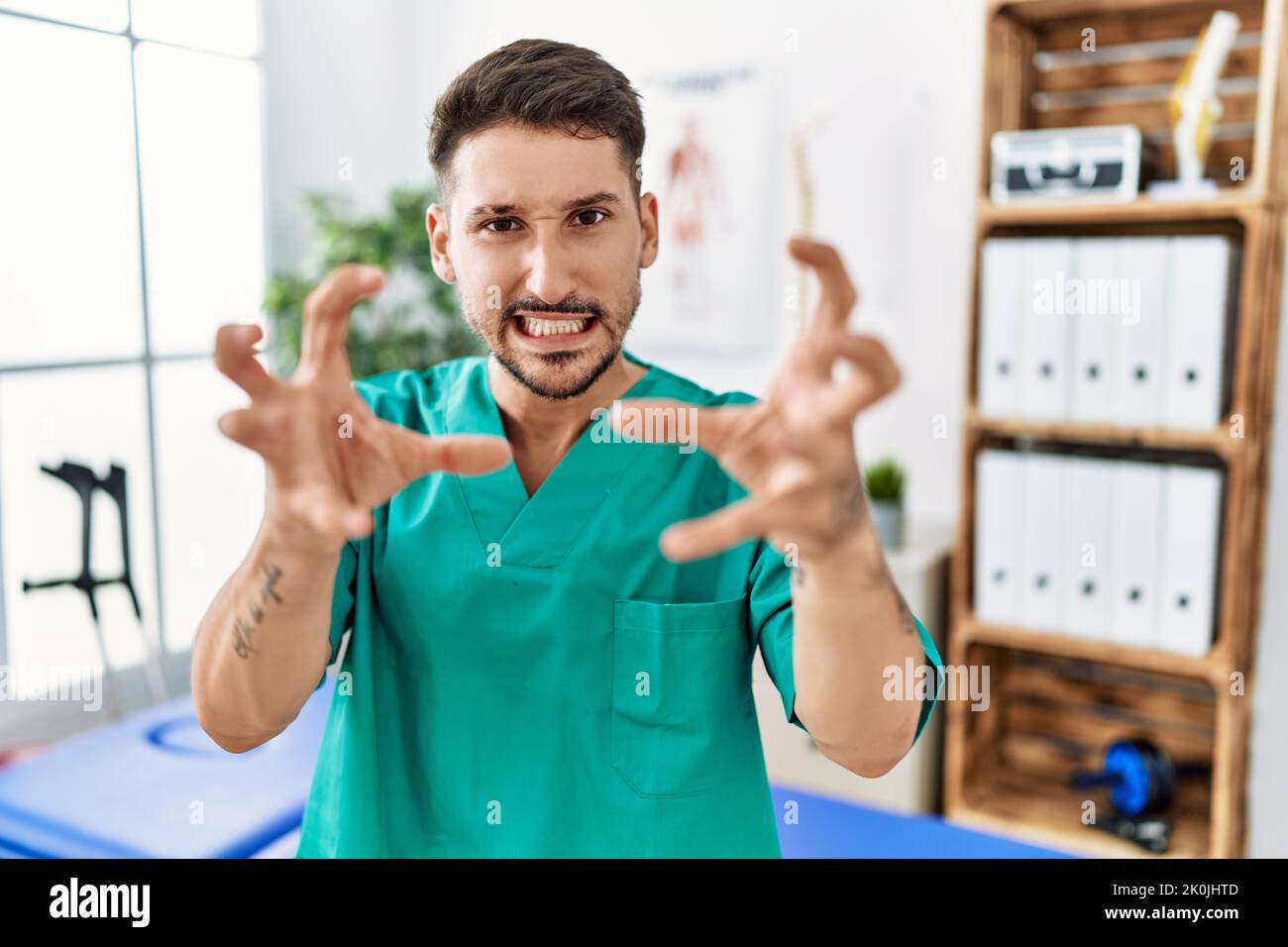 Young physiotherapist man working at pain recovery clinic shouting ...